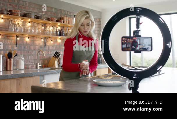 Woman piping icing from pastry bag onto cookies in kitchen filming ...
