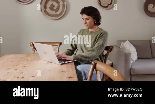Woman typing on silver laptop in dining area, seeing funny message on ...