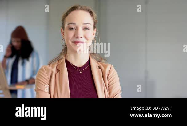 Female colleague hearing man speaking on phone at desk and wearing blazer while smiling ...
