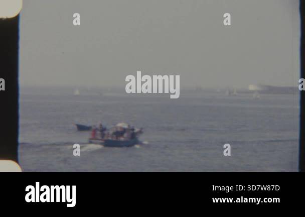A small boat with people aboard sails across a calm sea, captured on ...