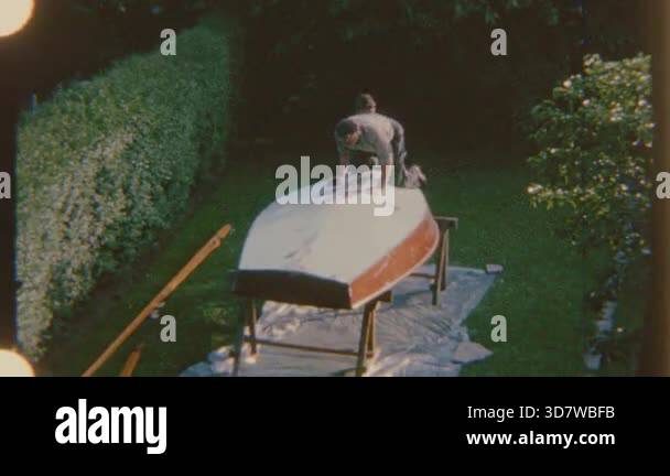 Two men work on a small boat resting upside down on sawhorses in a ...