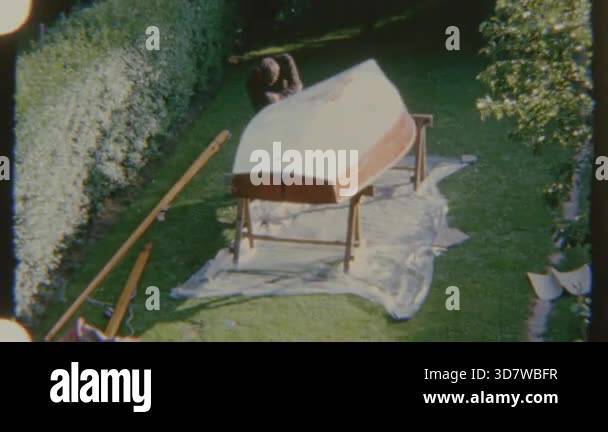 A young man works on a small boat resting upside down on sawhorses in ...