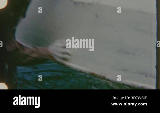 A man sands the hull of a boat, captured up close on 8mm film, focusing ...