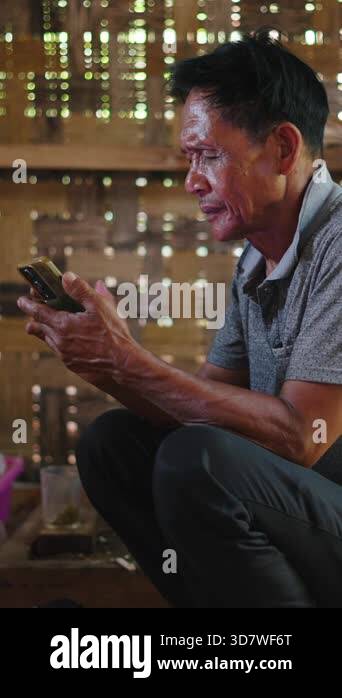 Senior man using mobile phone in his rustic bamboo house interacting ...
