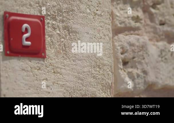 A bright red number sign is mounted on a rough stone wall under ...