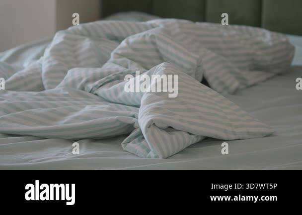 Soft blankets and sheets are twisted and tossed on a bed showing ...