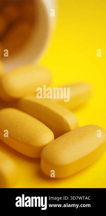 Yellow tablets are scattered from a white container on a yellow surface ...