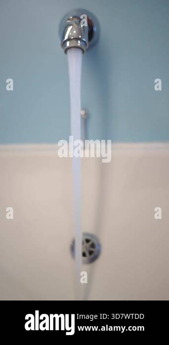 Water streams from the faucet into a clean bathtub with a simple design ...