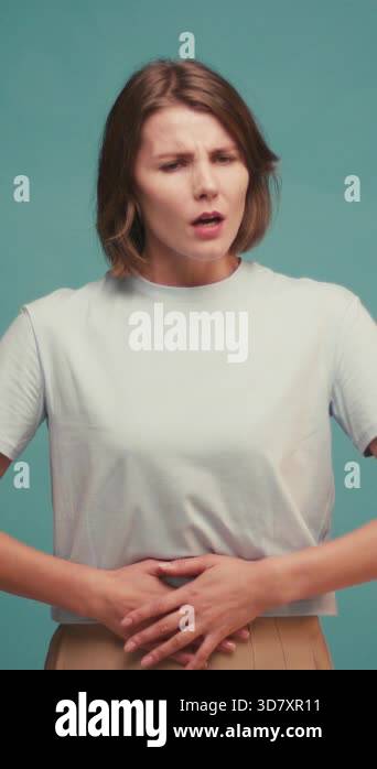 Upset young Hispanic woman feeling belly abdomen pain on blue ...