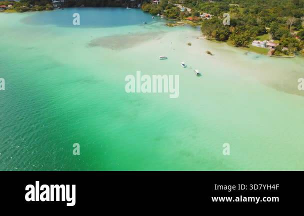 Boats anchored in shallow turquoise water near shore of Bacalar lagoon ...