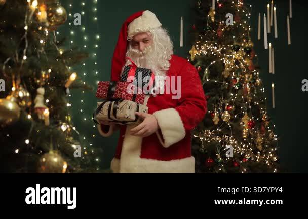 Santa Claus steps forward holding a bundle of wrapped gifts as ...