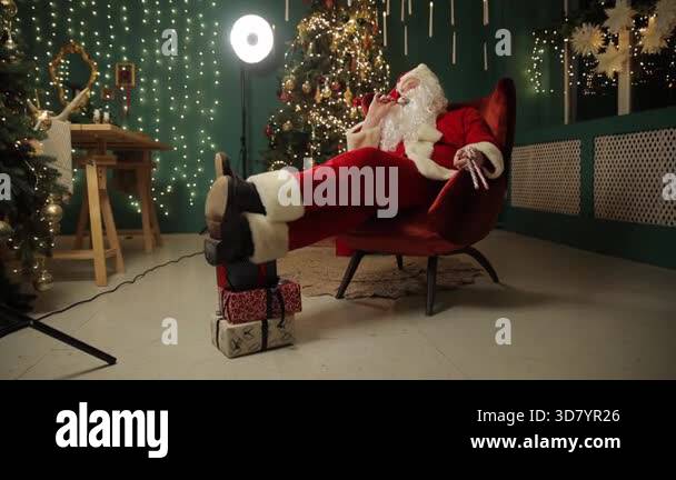 Santa Claus leans back in a chair with legs crossed, taking a quiet ...
