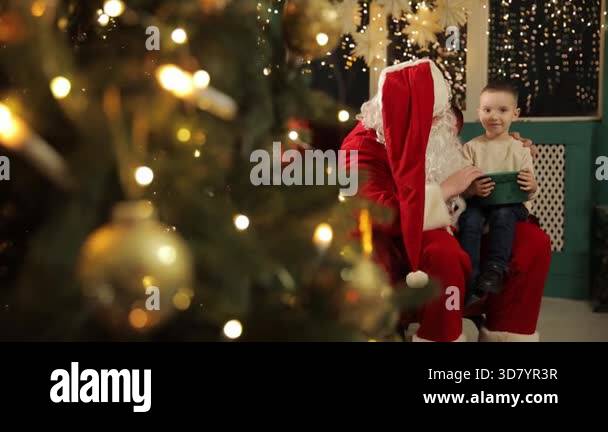 Santa Claus sits with a boy near a glowing Christmas tree, captured ...