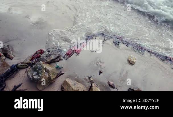 close up of a foamy wave washing over plastic trash and rocks littering ...