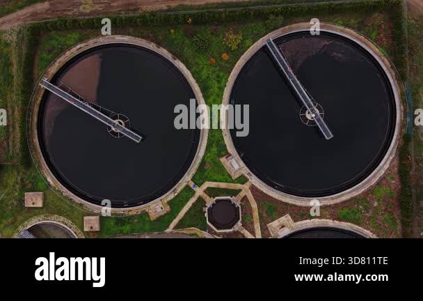 Aerial view of two large circular tanks at a water treatment facility, surrounded by greenery ...