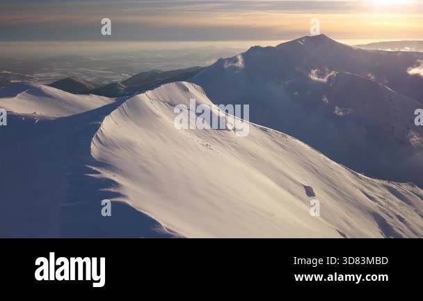 Aerial view of snowy Alpine mountains at sunrise. Golden morning light ...