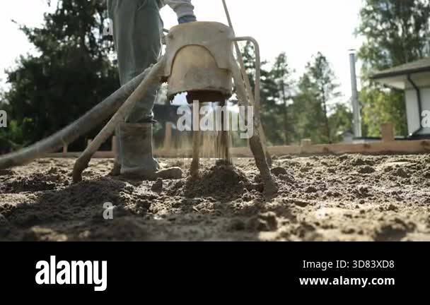 Worker levels wet concrete on rooftop slab with pump and chute. Low ...
