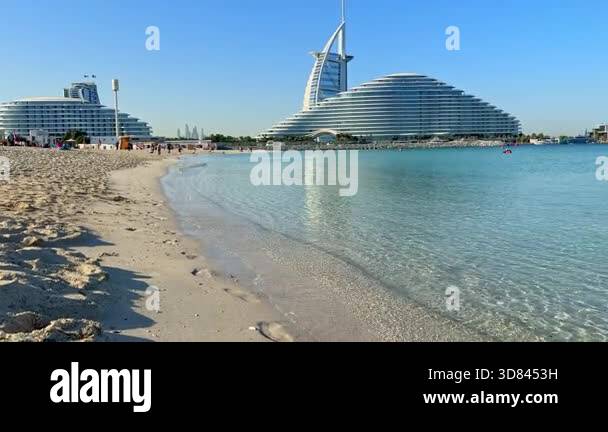 Beautiful beach scene in Dubai with waves rolling onto the shore, clear blue sea, and Dubai ...