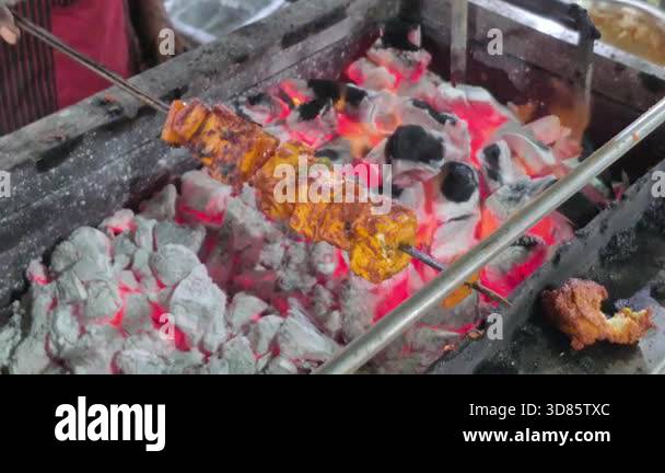Closeup of a chef roasting paneer kebabs over coal and fire at a ...