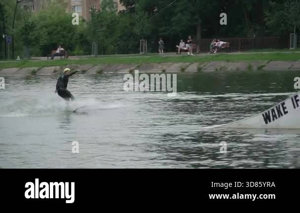 A male athlete black wetsuit yellow helmet holds onto rope one hand and ...