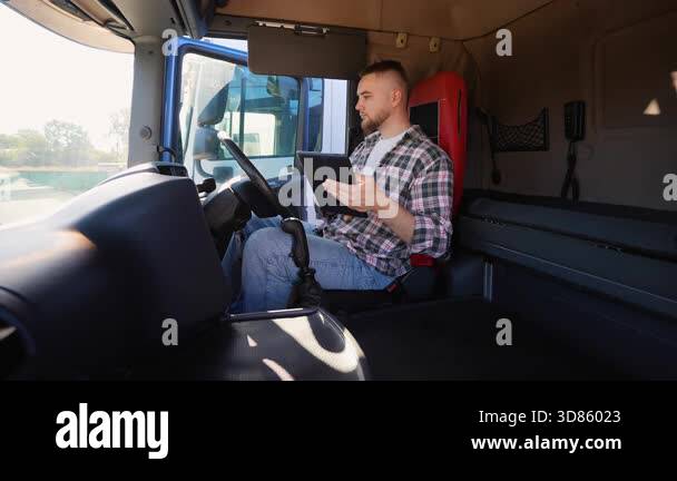 Young male lorry driver sitting inside a truck cabin and using a ...
