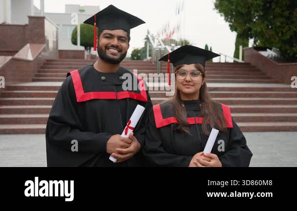 Happy indian graduate couple in academic gowns and caps holding ...