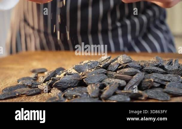 sprinkling sunflower seeds on wooden board, hands in striped apron ...