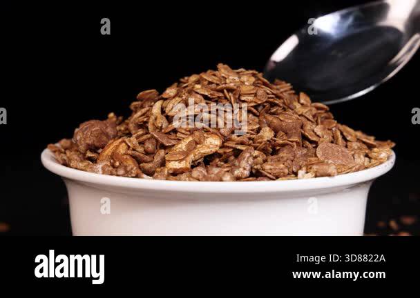 A spoon drops granola into a bowl against a black background ...