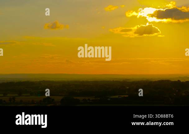 Evening sun glowing through soft clouds above distant farmland. Warm ...