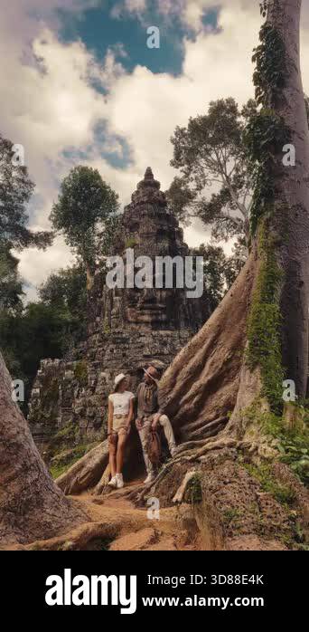 Travel couple posing on tree roots in front of Victory Gate, Bayon ...
