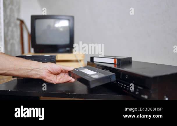 Hand holding VHS cassette by TV. A person holds a VHS tape near a ...