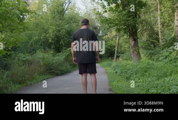 A man walks along path in green spring forest, limping on one leg, 4k ...