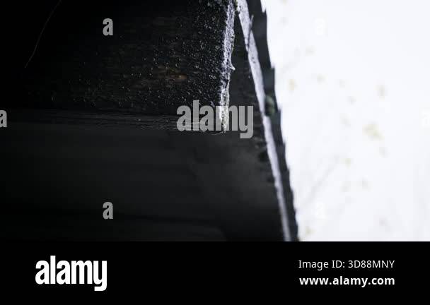 A close-up of heavy rain dripping from black wooden roof eaves during a ...