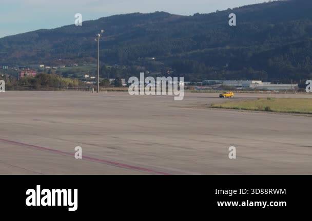 Yellow maintenance vehicle taxis on a wide runway with mountains and ...