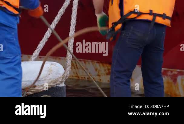 Dock worker pulls heavy mooring ropes along wet concrete pier ...