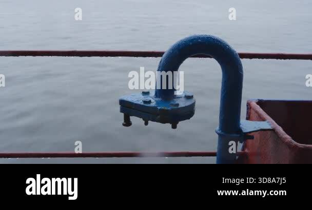 Curved metal bollard rises from wet deck. Calm water reflects smooth ...