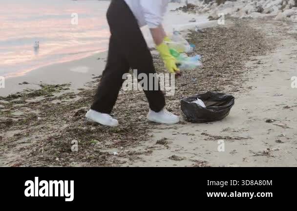 Volunteer cleaning plastic trash on a polluted beach, picking up ...