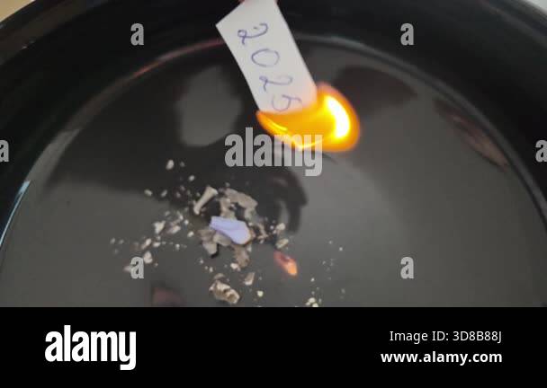 hand burning 2025 paper over plate close-up of hand holding small note ...