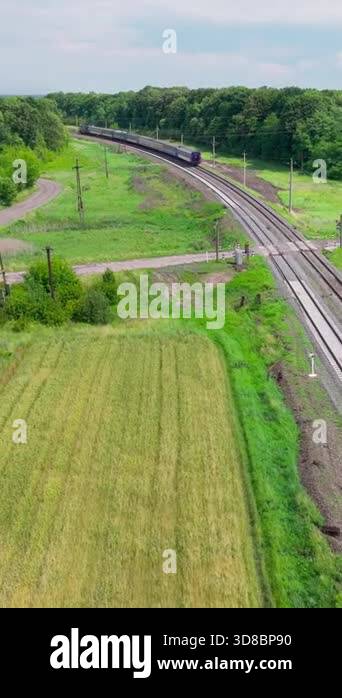 Vertical video. Passenger train moves along double railway across wide ...
