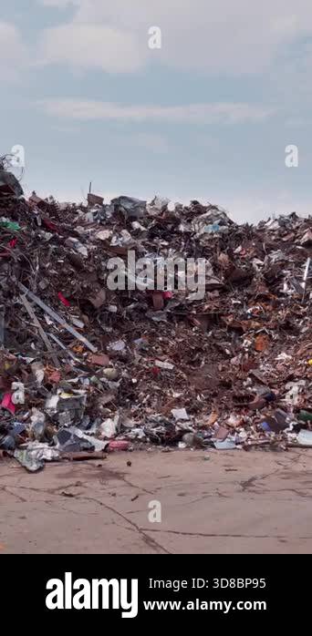 Vertical video. Large mound of scrap metal stands in recycling yard by ...