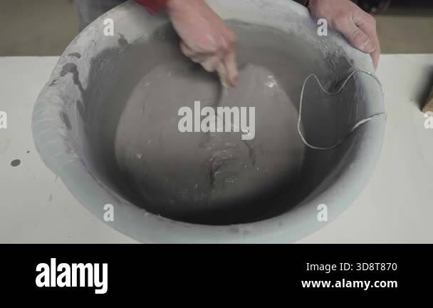 Professional ceramist mixing grayish liquid in metal bucket while ...