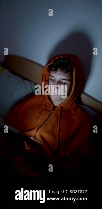 Teenager boy using a smartphone lying in bed late at night, playing ...