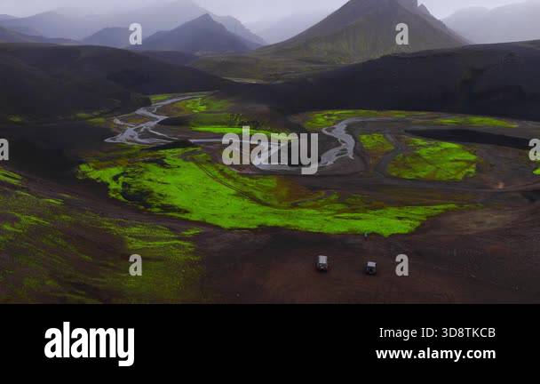Aerial view shows black volcanic slopes, braided river, and neon green ...