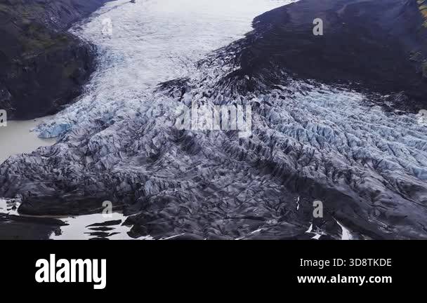 High aerial shot shows a broad crevassed glacier in Iceland, ash ...