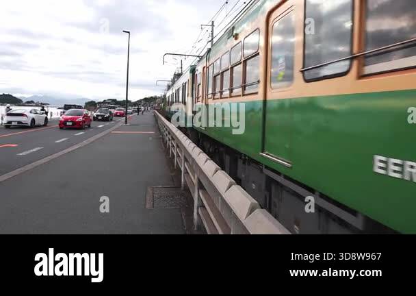Vintage green and cream Enoden train 305 and 355 passes on coastal tracks by Route 134 and a ...