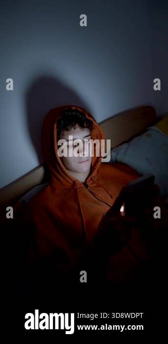 Teenager boy using a smartphone lying in bed late at night, playing ...