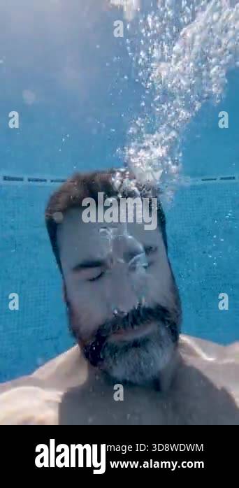 Bearded man with closed eyes releases air bubbles underwater in a ...