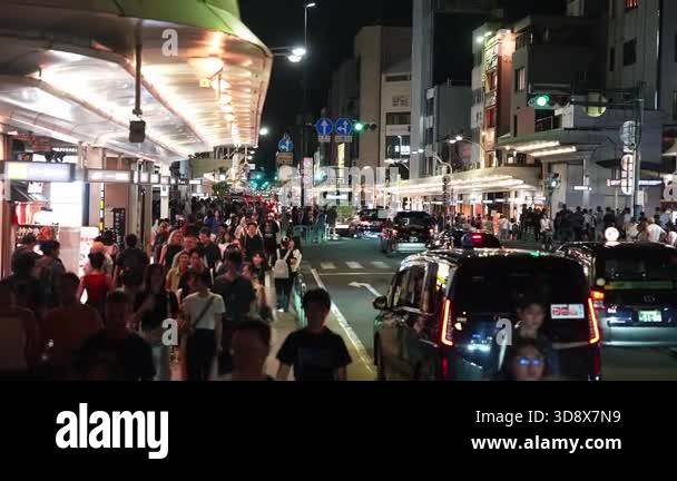 Night street in downtown Kyoto shows crowds under a curved lit canopy ...