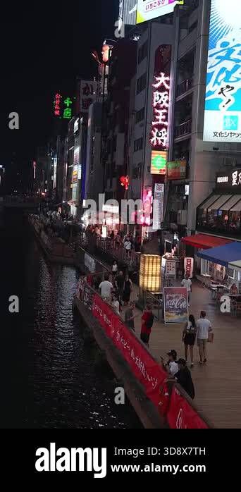Night view of Dotonbori canal in Osaka, Japan, locals and tourists stroll on a crowded boardwalk ...