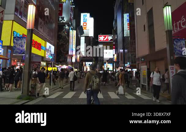 Pedestrians cross a wide avenue in Akihabara, Tokyo at night. Laox sign ...